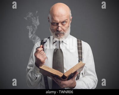 Confident senior professor smoking a pipe and reading an old book ...