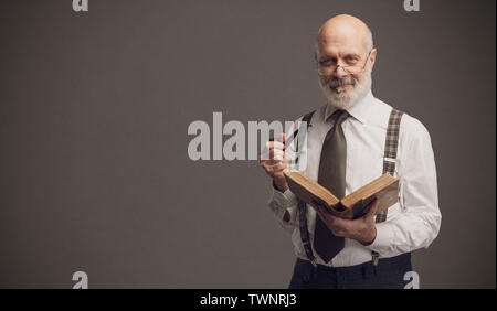 Confident senior professor smoking a pipe and reading an old book ...