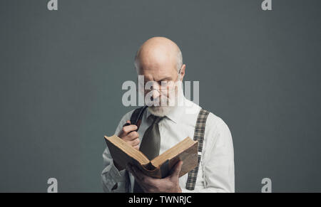 Confident senior professor smoking a pipe and reading an old book ...