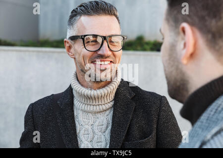 Two handsome men wearing coats spending time outdoors, using mobile ...