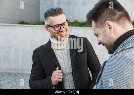 Two handsome men wearing coats spending time outdoors, using mobile ...