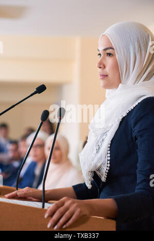 Confident young Muslim female politician in hijab speaking into ...