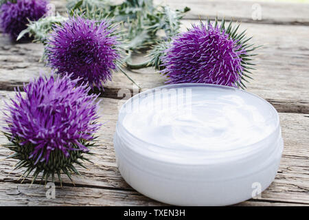Thistle flower with open jar of cosmetic face cream on wooden ...