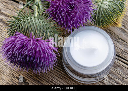 Thistle flower with open jar of cosmetic face cream on wooden ...