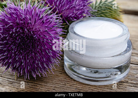 Thistle flower with open jar of cosmetic face cream on wooden ...