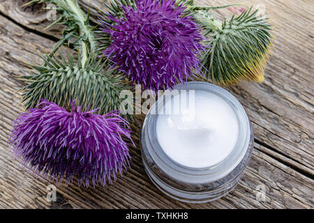 Cream with flowers thistle on wooden background. Medicinal plant ...