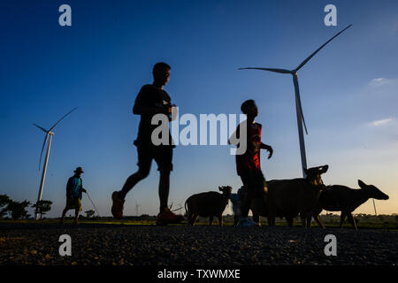 Residents walk past the turbines on Tolo 1Jeneponto wind energy power ...