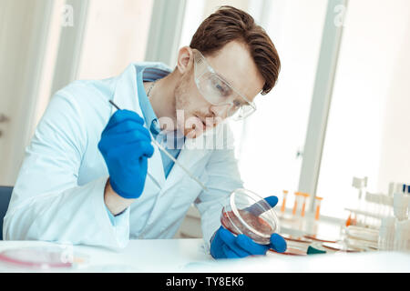 Worker, wearing special protective gloves and glasses, using grinder to ...