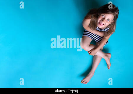 Child on plain blue background looking at camera sitting. Girl glancing ...