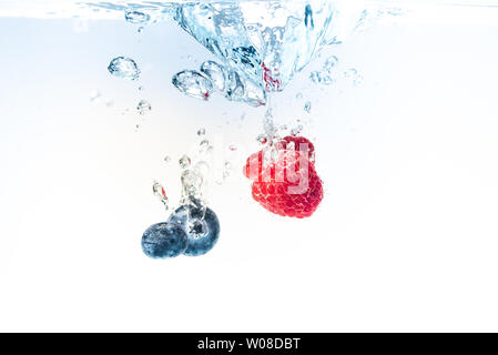 Blueberry?s and raspberries splashing into crystal clear water with air ...