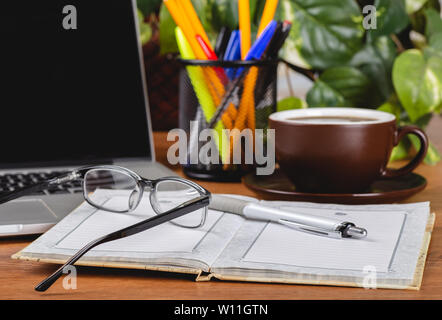Notebook with pen, pencil holder and cup of coffee on black background ...