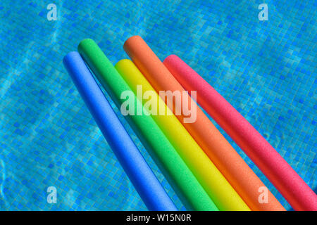 Brightly coloured pool noodles and swimming pool, with copy space. Fun ...