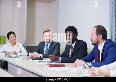 Confident multi-ethnic broker in casualawear and eyeglasses talking to ...