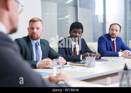 Confident multi-ethnic broker in casualawear and eyeglasses talking to ...