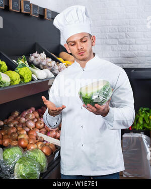 Satisfied pleasant smiling male cook choosing vegetables in grocery ...