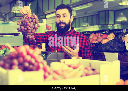Shop assistant demonstrating grapes in grocery shop Stock Photo - Alamy