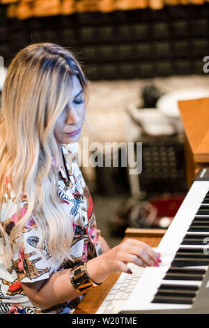 Blonde female musician playing keyboards in a musical studio while ...