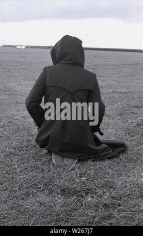 woman in a black raincoat with a hood approaches a young girl who is ...