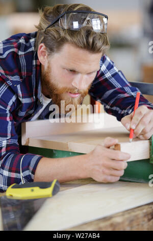 Handsome carpenter working with a wood, marking plank with a pencil in ...