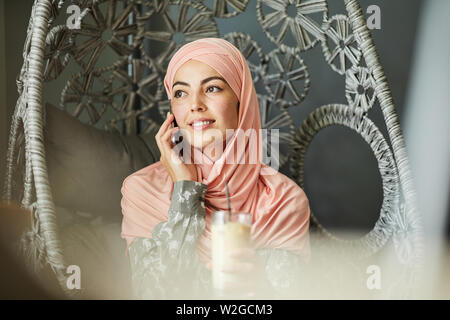 Young pretty Muslim woman with glass of coffee resting in chair and ...
