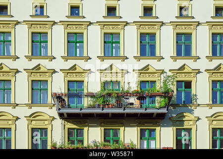 Yellow apartment building facade with green tree branches in sunlight ...