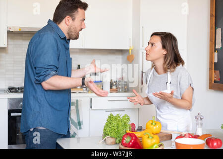 Young couple arguing in kitchen. Frustrated wife with rolling pin ...