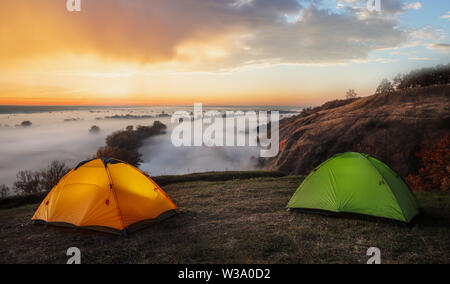 Dramatic sunset over the river and tents with a fire. The orange and ...