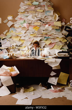 Overworked businessman sitting at a messy desk in office, light effect ...