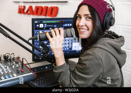 Beautiful happy young female radio host using microphone and headphones ...