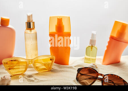 Bottles of sunscreen with sunglasses on sand against white background ...