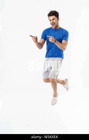 cheerful young man pointing with fingers while looking away on blue ...