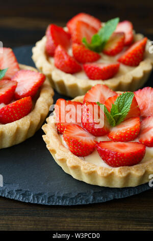 Tartlets with custard, strawberries and mint served on a slate plate ...