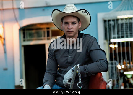 A young good-looking Cuban cowboy sits with his book of tours and ...