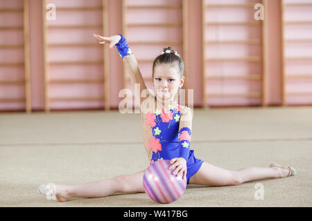 Little girl doing gymnastics with hoop, ball and split isolated on grey ...