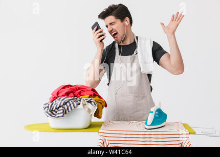Handsome angry brunette houseman wearing apron standing isolated over ...