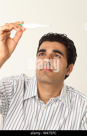 Cold symptom. Young man checking temperature with thermometer at home ...