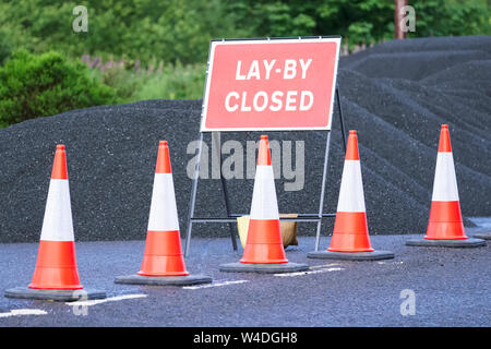 Road lay by closed sign with pile of black tar and red traffic cones ...