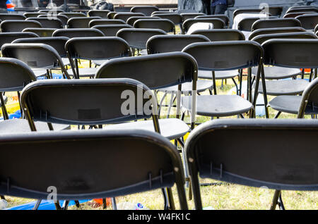 rows of empty black folding chairs in a large event hall with dark ...
