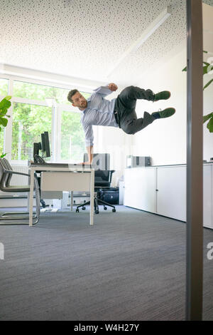 Businessman doing a one-handed handstand on desk in office Stock Photo ...