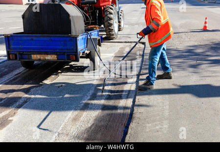 The road maintenance worker sprays the bitumen mixture onto the cleaned ...
