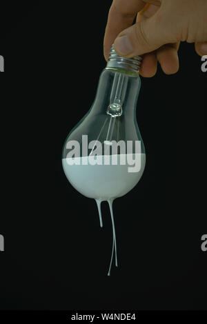 Hand holding big light bulb with dripping white paint on a black ...