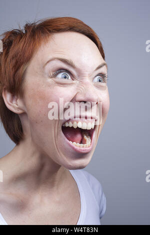 Young redhead woman shouting and screaming loud to side with hand on ...