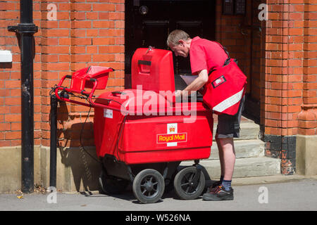 A postman collects mail for delivery from an electric postal round ...