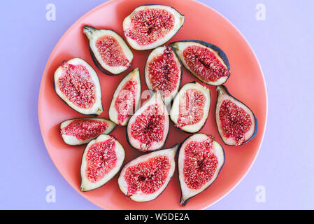 Ripe cutted figs on coral plate on violet background. Copy space. Top ...