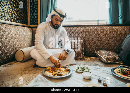 Arabic man with traditional clothes eating chicken mandy, in Dubai ...