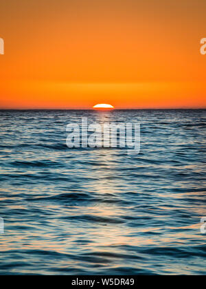 Half sun below horizon over blue sea waves, beautiful sunset over sea ...