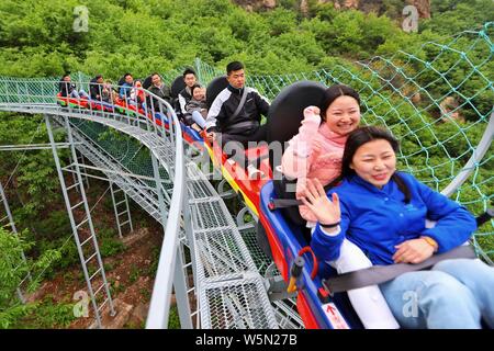 Tourists take a roller coaster ride cross over forests of the Fuxi ...