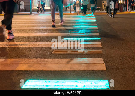 Pedestrians walk across a zebra crossing illuminated by LED lights in ...