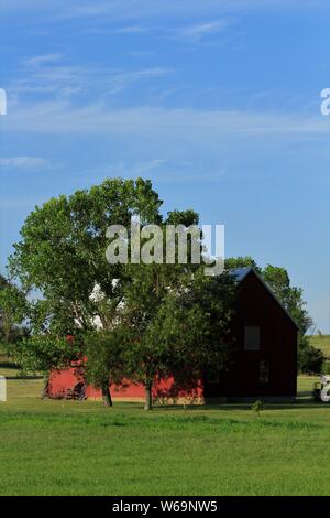 Kansas red and white barn with a fence and tree's with blue sky out in ...