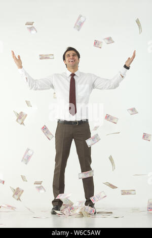 Money falling on a businessman standing with his arms outstretched ...